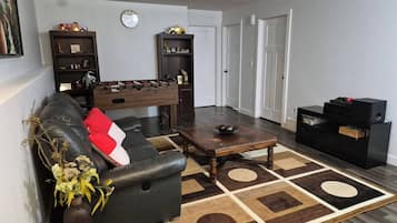 Uma sala de estar com sofá, mesa de centro, mesa de pebolim e estante de livros.