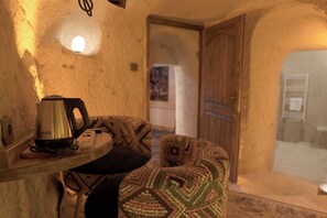Um interior acolhedor com uma parede de pedra rústica, uma pequena mesa com uma chaleira e uma almofada estampada.
