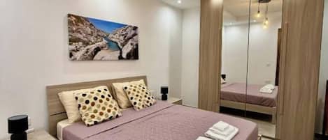 Quarto moderno com uma cama grande, mesa de cabeceira, espelho e um quadro na parede.
