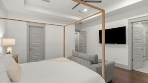 Quarto moderno com cama de dossel, sofá cinza, TV de tela plana na parede e closet espaçoso com portas deslizantes.