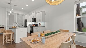 Cozinha moderna com armários brancos, mesa de jantar de madeira e vista para o exterior.