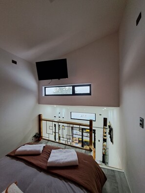 Quarto com cama, televisão presa na parede, janela e vista do andar de baixo.