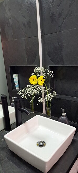 Casa de banho com lavatório branco, bancada preta e parede escura com uma faixa vertical branca.
