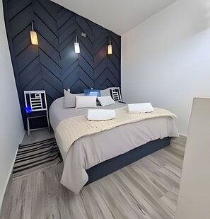 Quarto moderno com cabeceira em padrão herringbone, cama com roupa de cama branca e mesa de cabeceira com abajur.