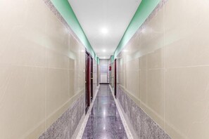 Corredor com piso de mármore e paredes com detalhes verdes, que leva a uma porta no final.