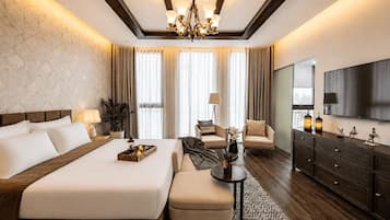 Quarto de hotel com cama grande, sofá, televisão e lustre.