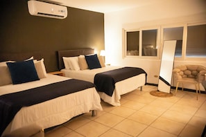 Quarto de hotel com duas camas, uma cadeira e uma janela com persianas.