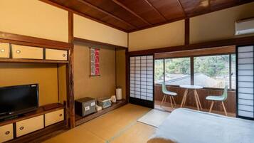 Quarto japonês tradicional com tatames, televisão, futon e portas deslizantes, com vista para o exterior.