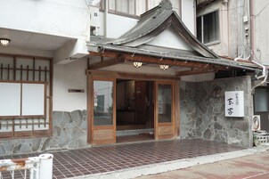 Um edifício japonês tradicional com entrada em azulejos, portas de madeira e parede de pedra.