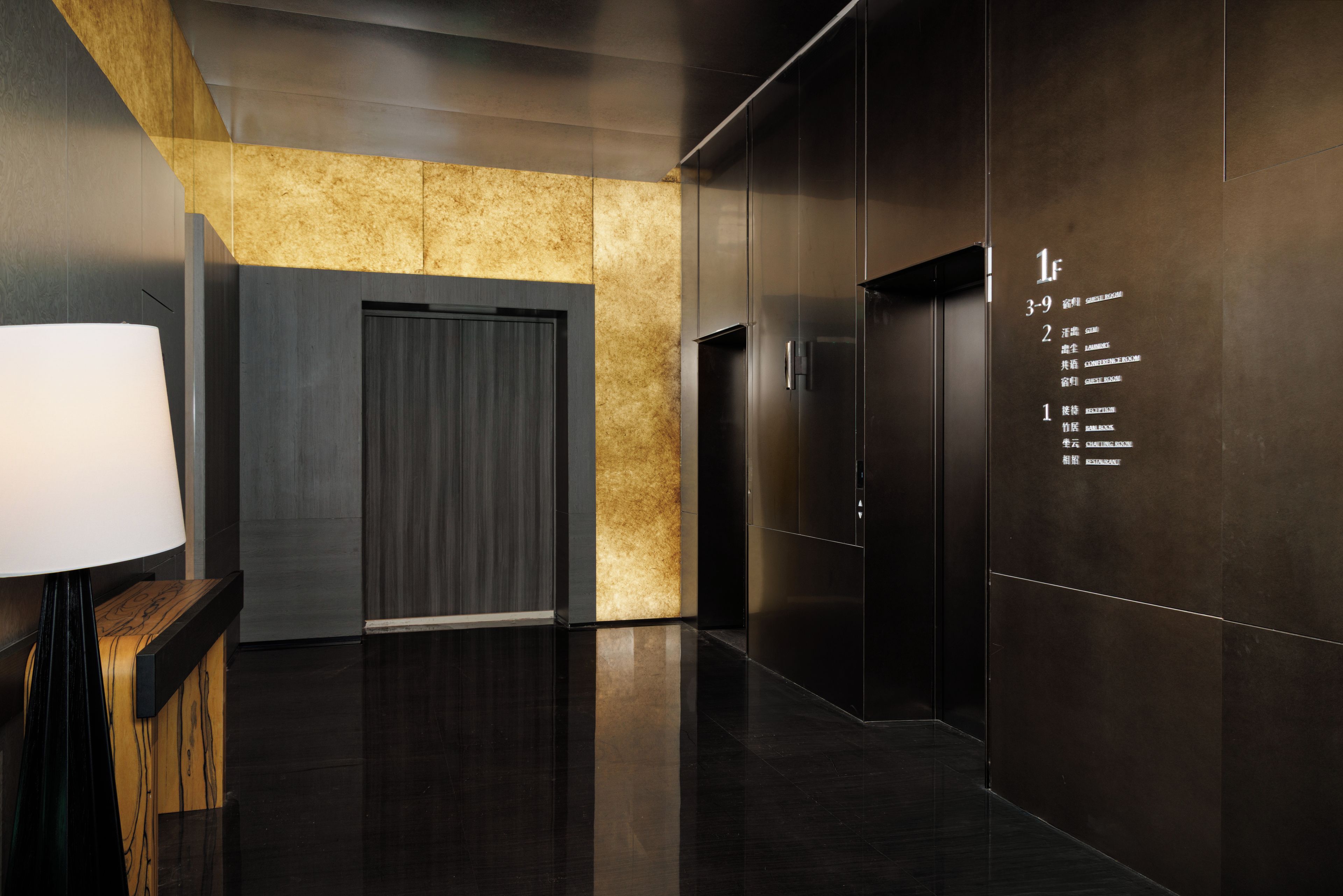 Interior moderno de elevador com visor digital exibindo números e nomes de quartos.