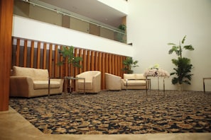 Um hall com carpete estampado, sofás bege, uma mesinha e um vaso de planta.