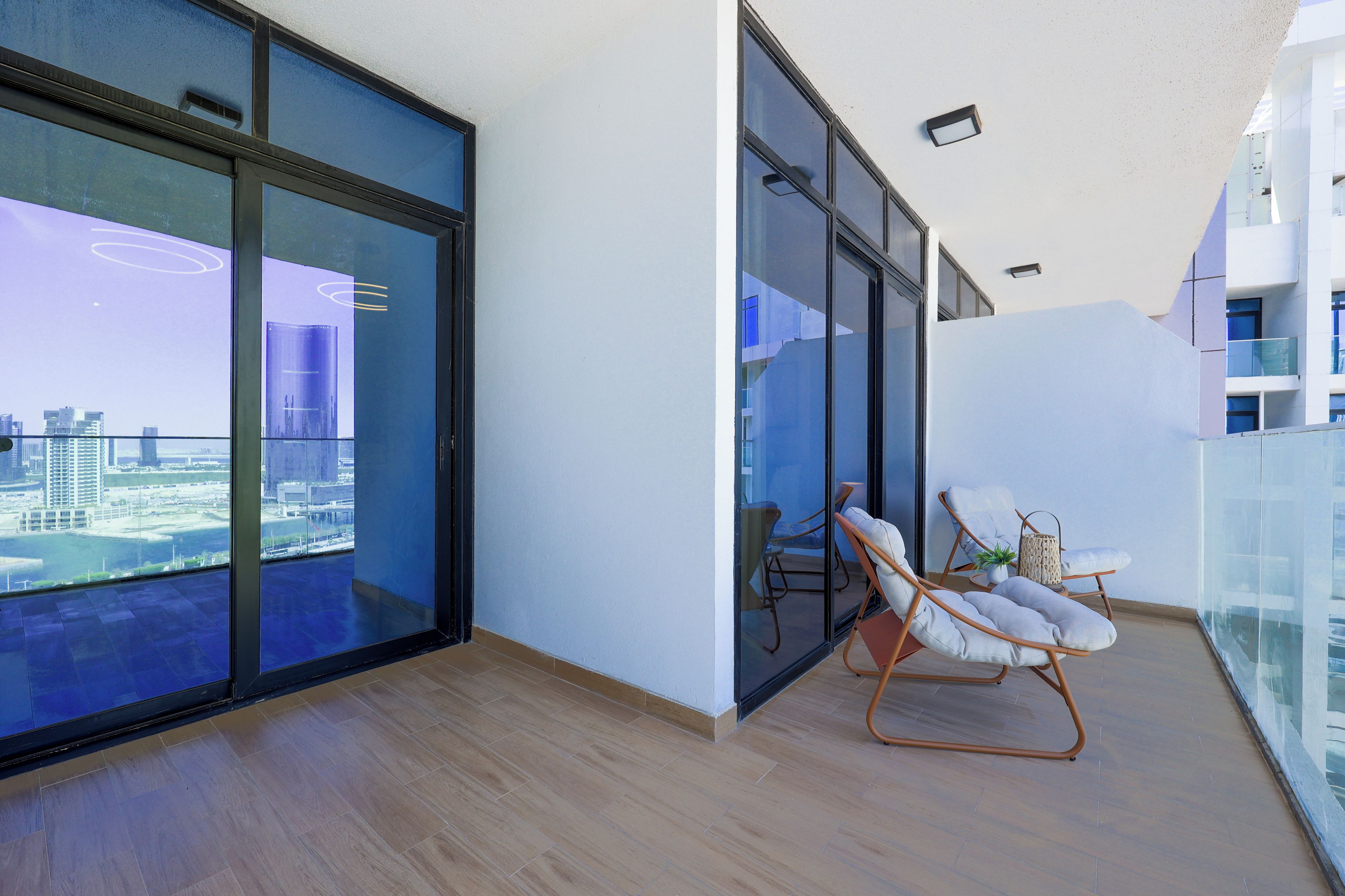 Varanda moderna com vista para a cidade, porta de vidro e área de estar com uma cadeira e mesa pequena.