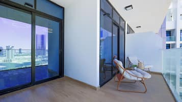 Varanda moderna com vista para a cidade, porta de vidro e área de estar com uma cadeira e mesa pequena.