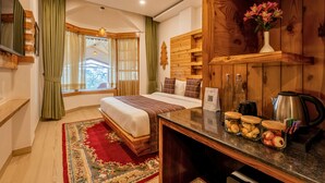 Quarto de hotel com cama, armário de madeira, área de refeições com chaleira e janela com cortinas.