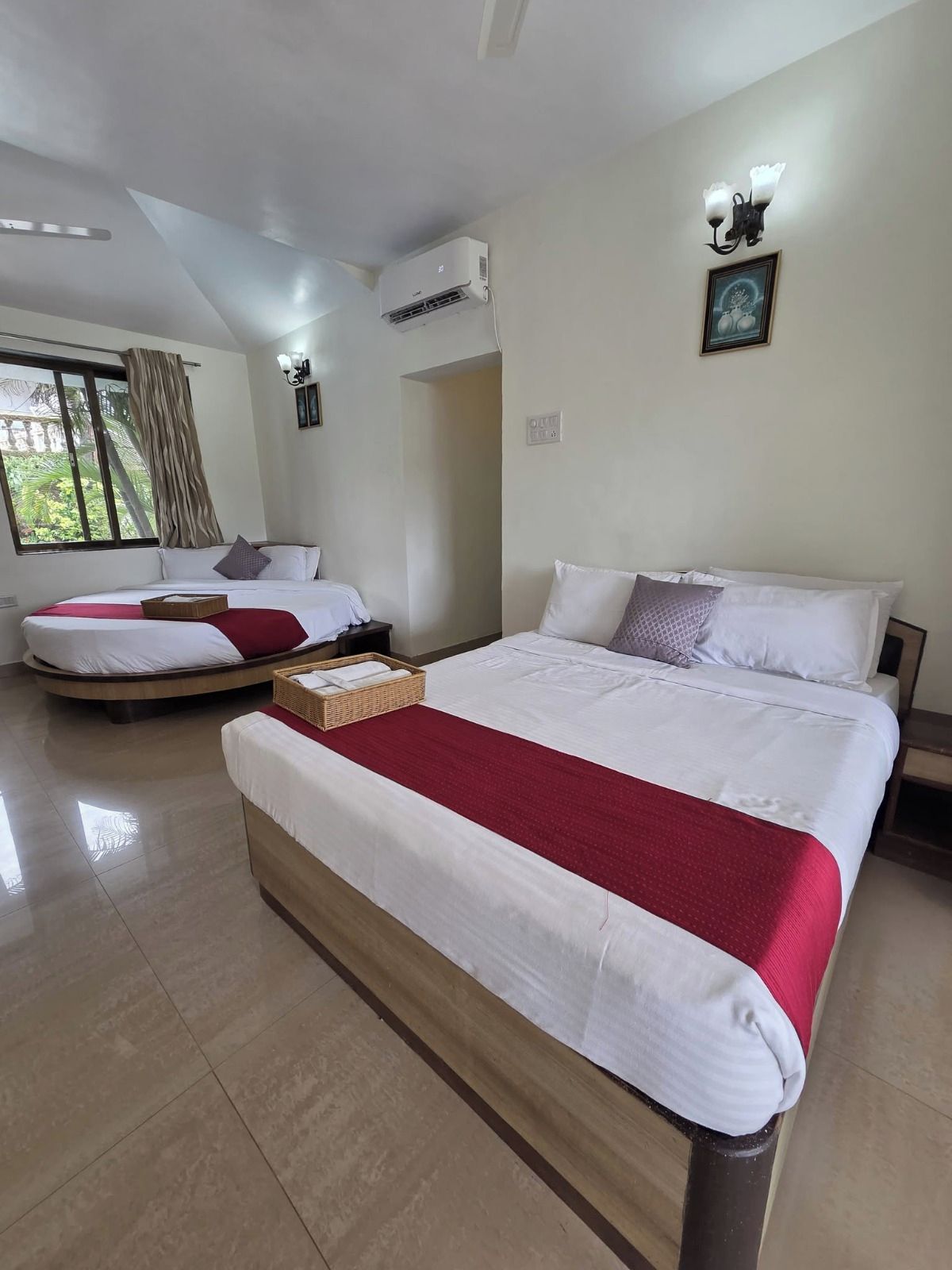 Quarto de hotel com duas camas, uma janela grande com cortinas, ar-condicionado fixado na parede e um quadro emoldurado.