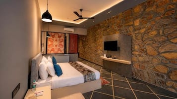Quarto moderno com parede de pedra, cama com almofadas, mesa de cabeceira, TV de tela plana e ventilador de teto.
