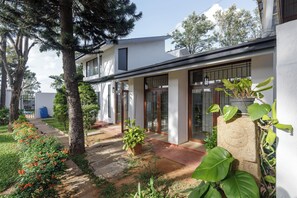 Uma casa moderna com varanda coberta, jardim com plantas floridas e uma grande árvore.