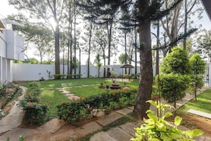 Um jardim com caminho pavimentado, diversas plantas e uma pequena construção.