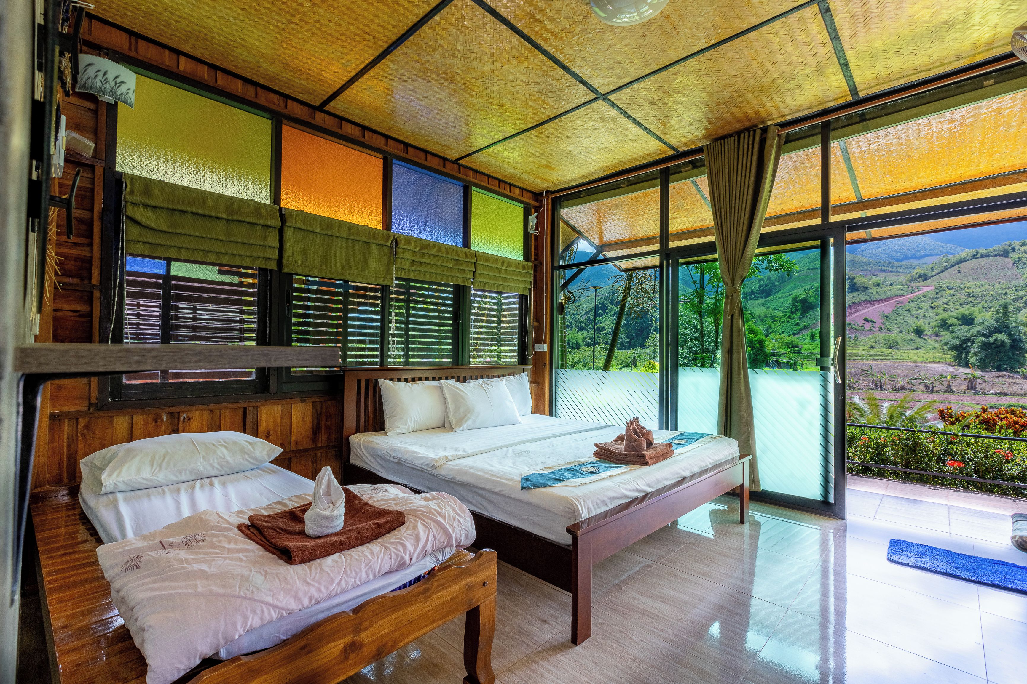 Quarto com duas camas, uma janela grande e vista para uma paisagem exuberante.