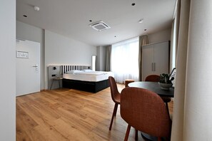 Quarto de hotel moderno com piso de madeira, uma cama, uma escrivaninha e uma cadeira.