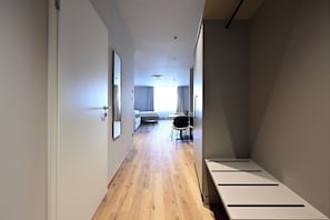 Quarto de hotel moderno com piso de madeira, uma cama, uma escrivaninha e uma cadeira.