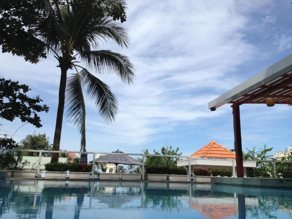 Piscina com céu claro, palmeiras e um edifício com telhado vermelho.