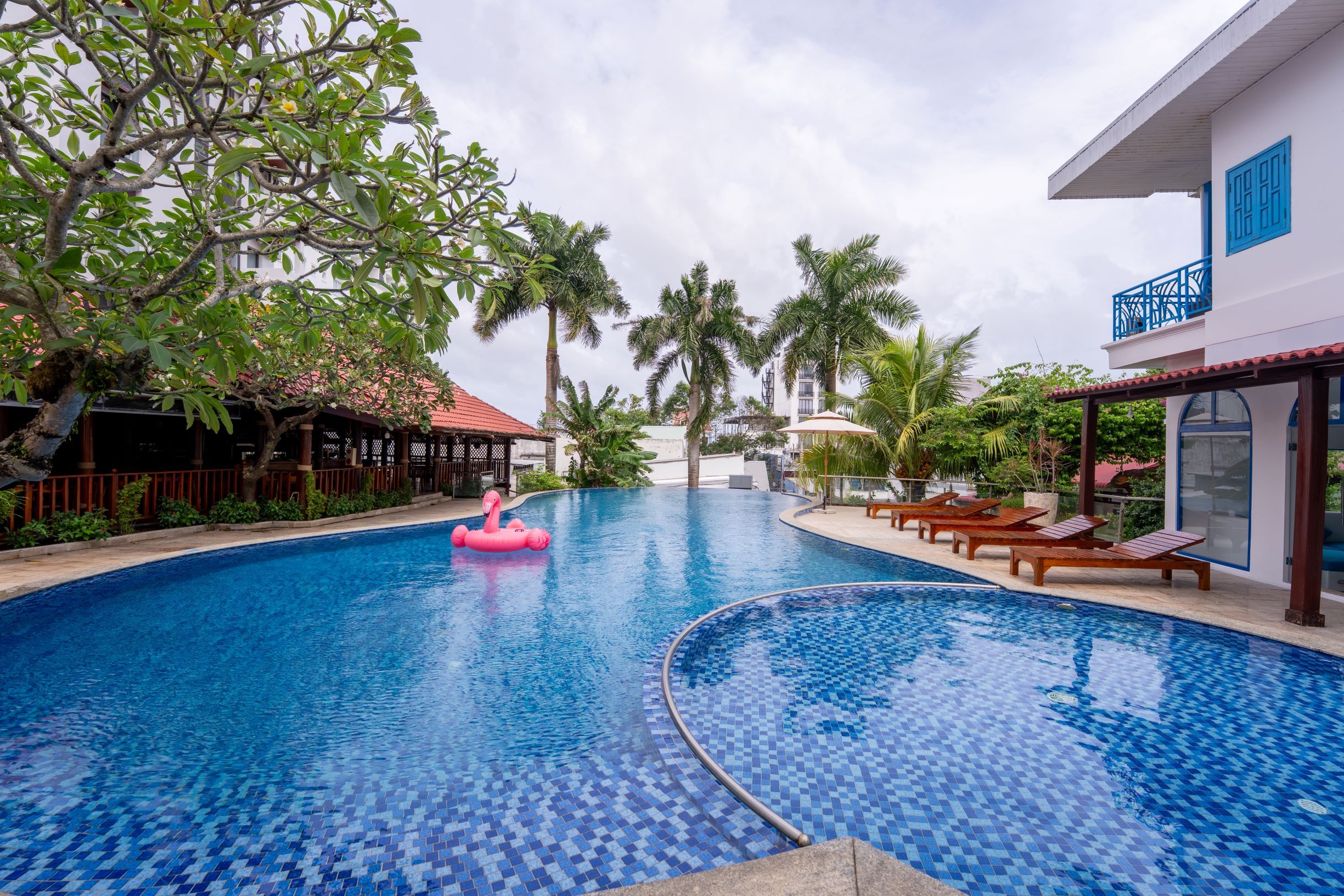 Uma piscina com um flutuador em formato de flamingo rosa, rodeada por palmeiras e espreguiçadeiras.