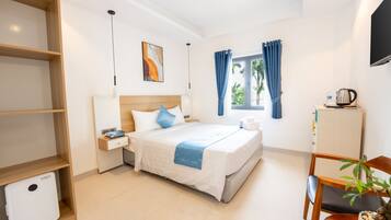 Quarto de hotel com cama, escrivaninha, cadeira, televisão e janela com cortinas.