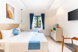 Quarto de hotel com cama, escrivaninha, cadeira, televisão e janela com cortinas.