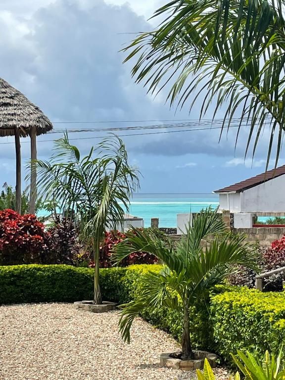 Um jardim com guarda-sol de palha, palmeiras e vista para o mar.