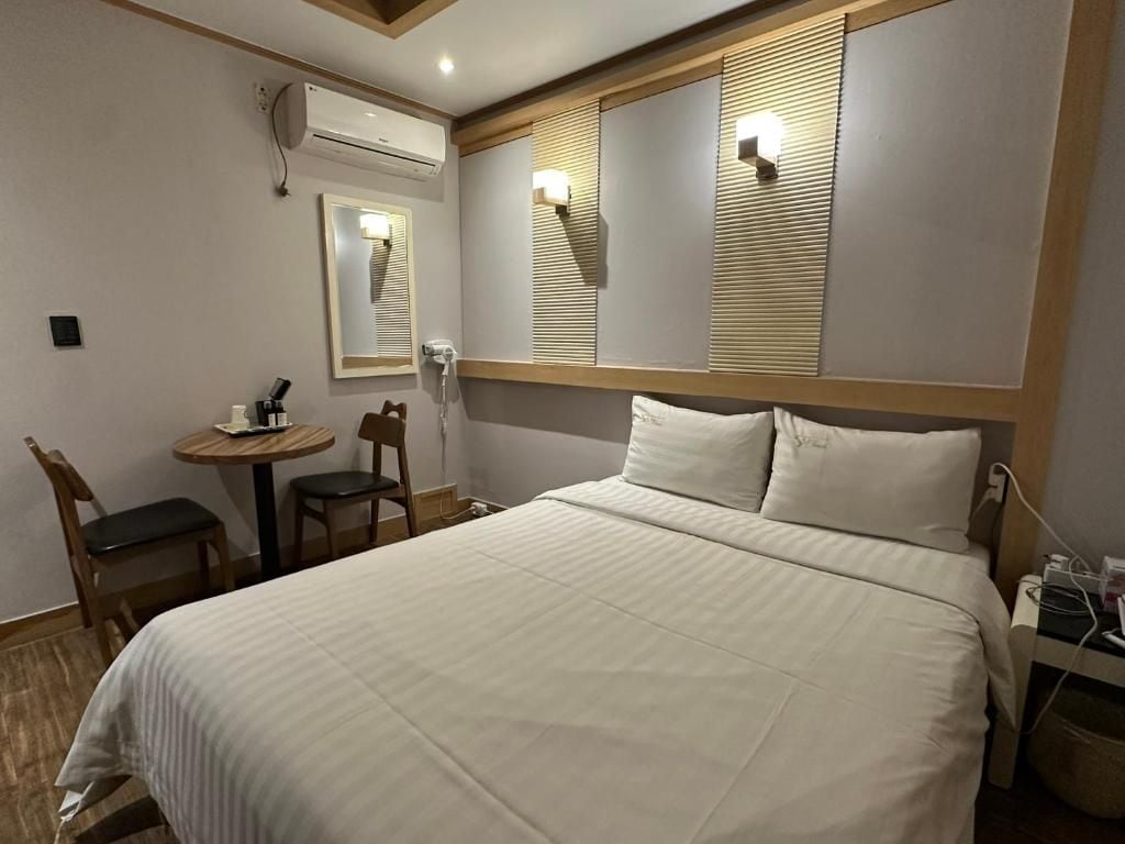 Quarto de hotel com uma cama grande, uma mesa pequena com cadeiras, um espelho e uma janela com persianas.