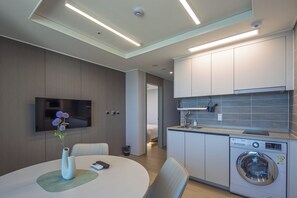 Quarto de hotel moderno com área de refeições, televisão, máquina de lavar e banheiro visível por uma porta aberta.