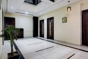 Um corredor limpo e moderno, com piso de azulejos brancos, portas de madeira escura e um vaso de planta.