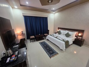 Quarto de hotel com cama, mesas de cabeceira, escrivaninha, cadeira, televisão e máquina de café.