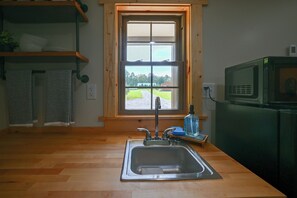 Cozinha com bancada de madeira, pia de aço inoxidável, janela com vista para o exterior e micro-ondas.
