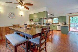 Espaço de refeições com mesa e cadeiras de madeira, ventilador de teto e cozinha ao fundo.