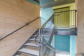Escadaria com guarda-corpos e corrimão metálicos, levando a uma porta com portão de metal.