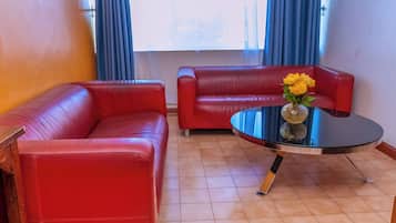 Um quarto com dois sofás de couro vermelho, uma mesa de centro de vidro com um vaso de flores amarelas e uma janela com cortinas azuis.