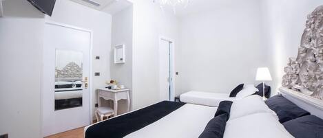 Quarto de hotel com cama, escrivaninha, poltrona, televisão e lustre.