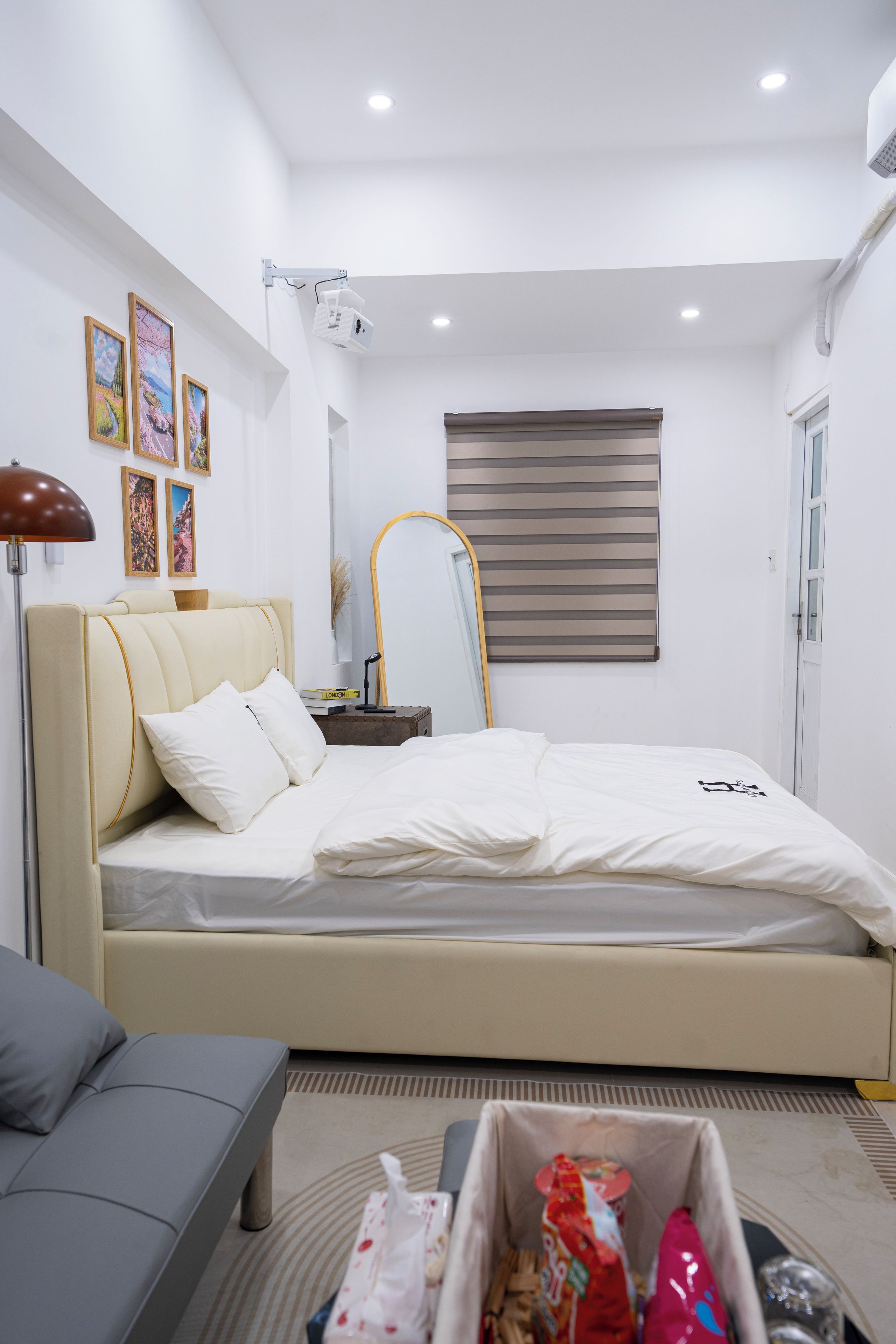 Quarto com cama, mesa de cabeceira, abajur e janela com persianas.