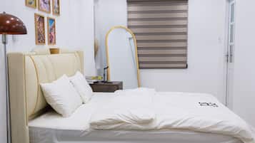 Quarto com cama, mesa de cabeceira, abajur e janela com persianas.