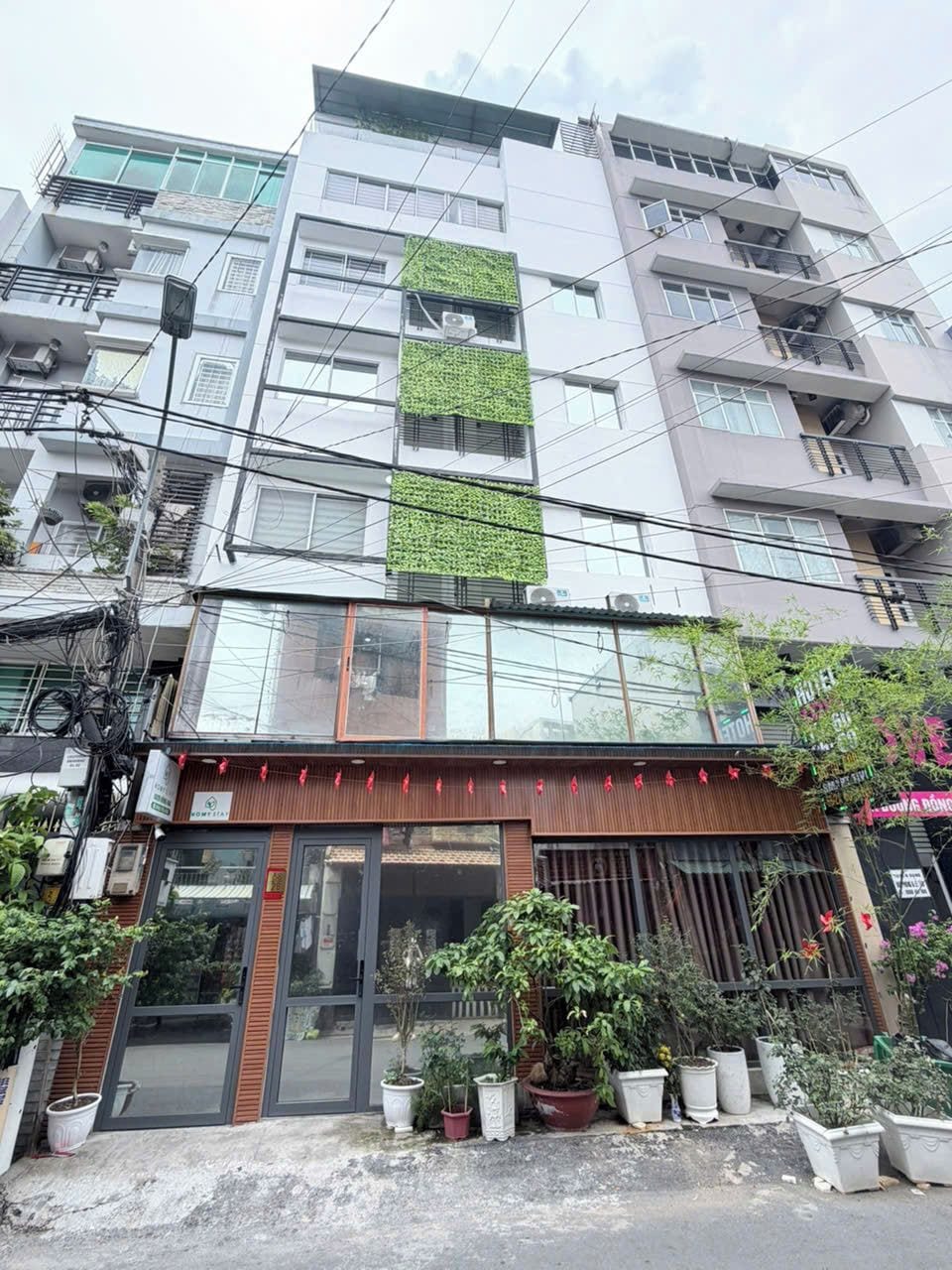 Edifício com vários andares, entrada no nível da rua, plantas em vasos e unidades de ar condicionado visíveis.