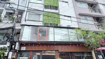 Edifício com vários andares, entrada no nível da rua, plantas em vasos e unidades de ar condicionado visíveis.