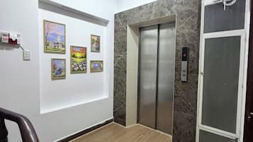 Um elevador moderno com visor digital, extintor de incêndio e detector de fumaça fixado na parede.