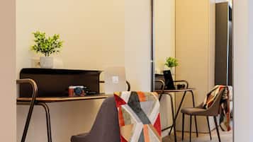 Quarto moderno com piso de madeira, uma escrivaninha com computador, uma cadeira com manta estampada e um espelho grande.