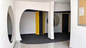 Um corredor com paredes brancas, piso de mármore e portas com detalhes em amarelo e preto.