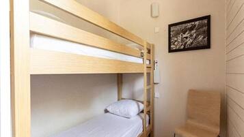 Uma cama de solteiro com estrutura de madeira, uma cama individual embaixo, uma cadeira e um aparelho de luz fixado na parede.