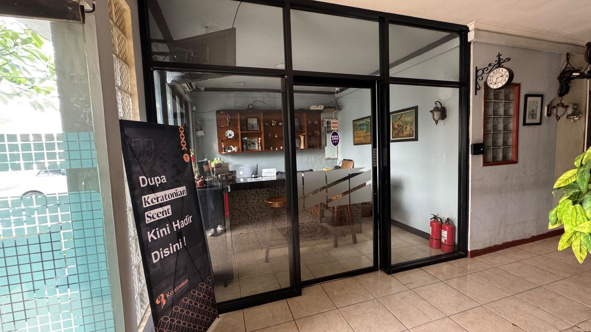Quarto com porta de vidro deslizante que dá para uma cozinha, uma placa preta com texto, um relógio na parede e um vaso de planta.