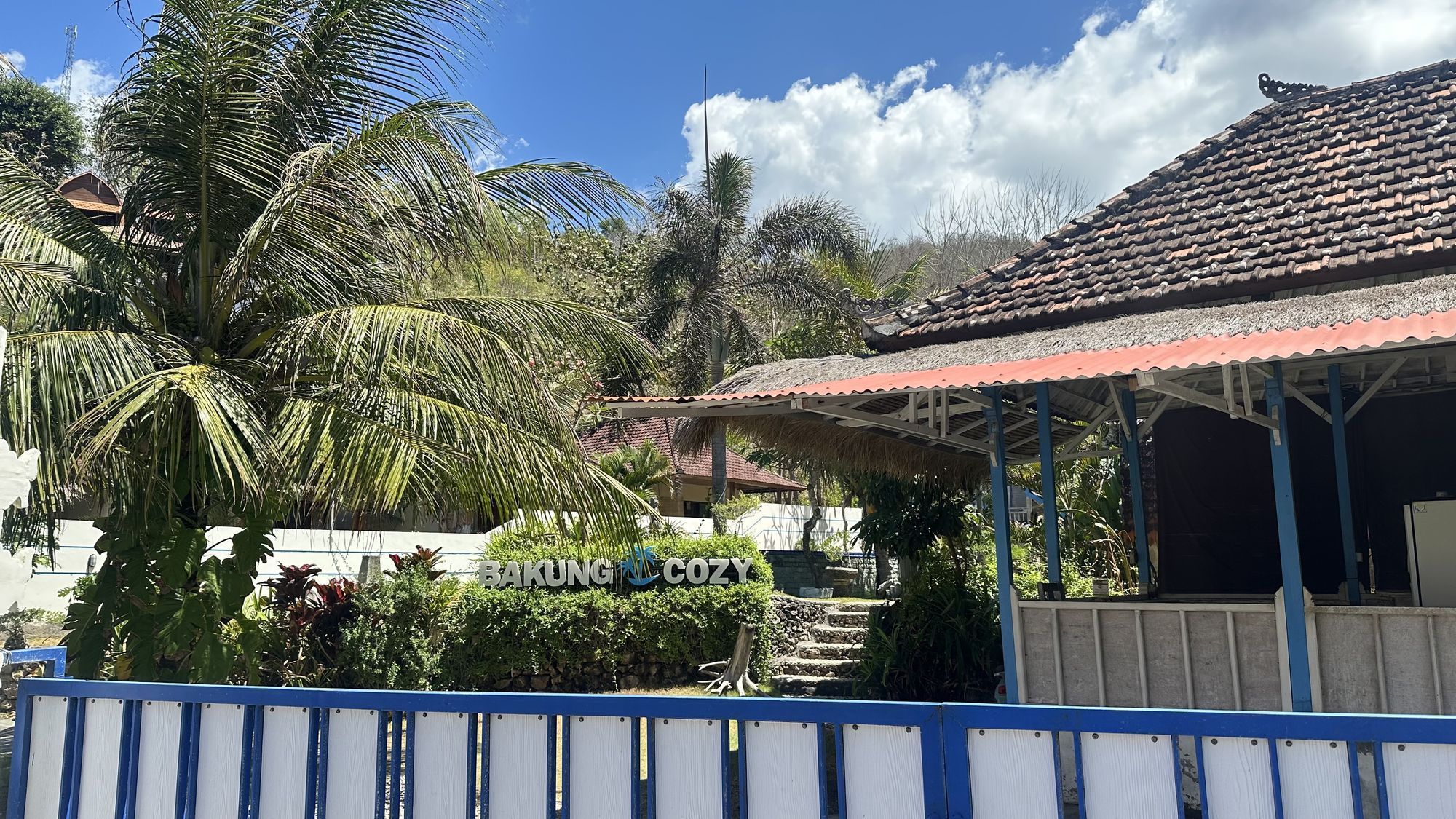 Um edifício com telhado de azulejos, cercado por palmeiras e um muro azul.