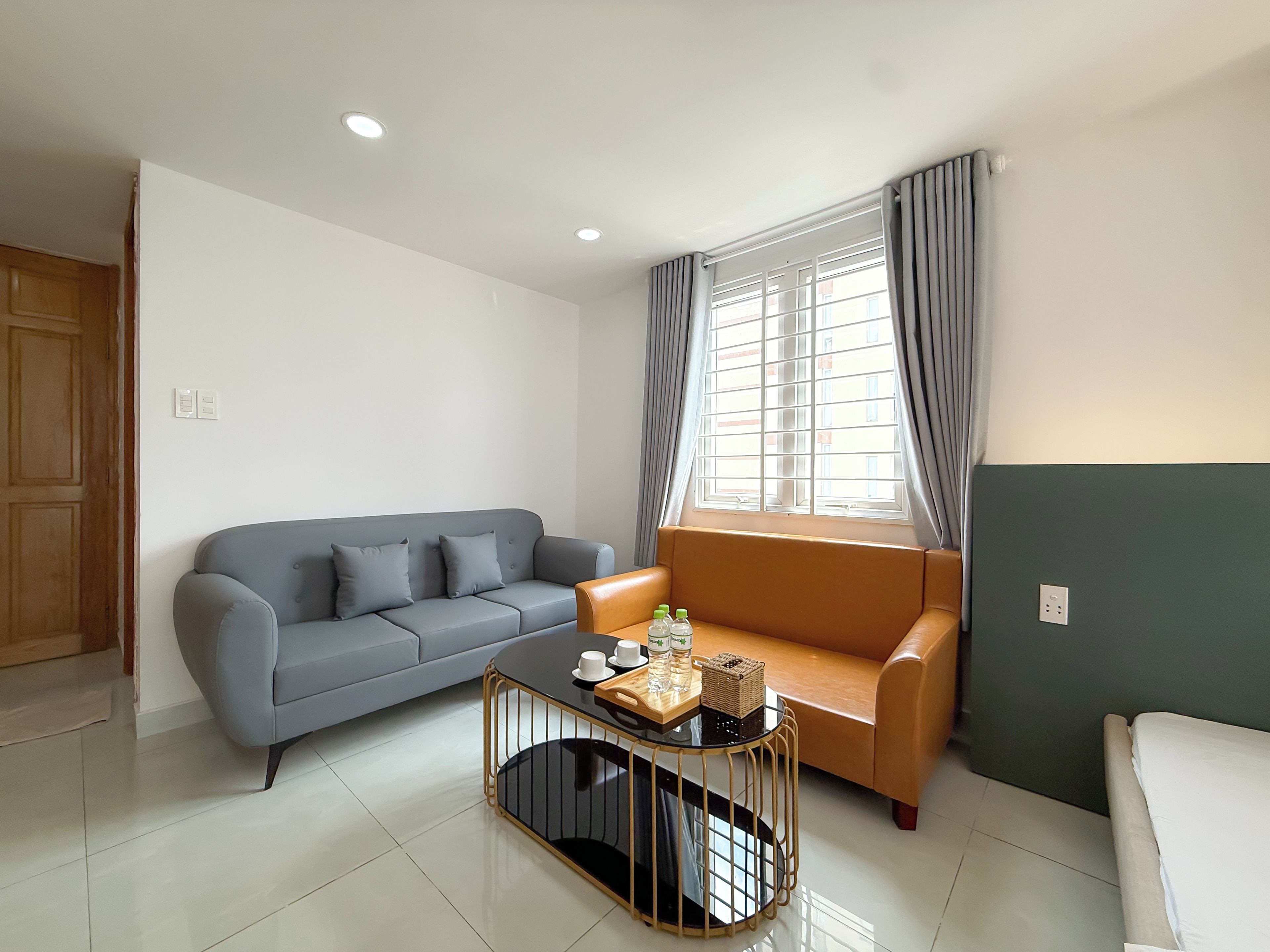 Uma sala de estar moderna com um sofá cinzento, um sofá castanho, uma mesa de centro de vidro e uma janela com cortinas.